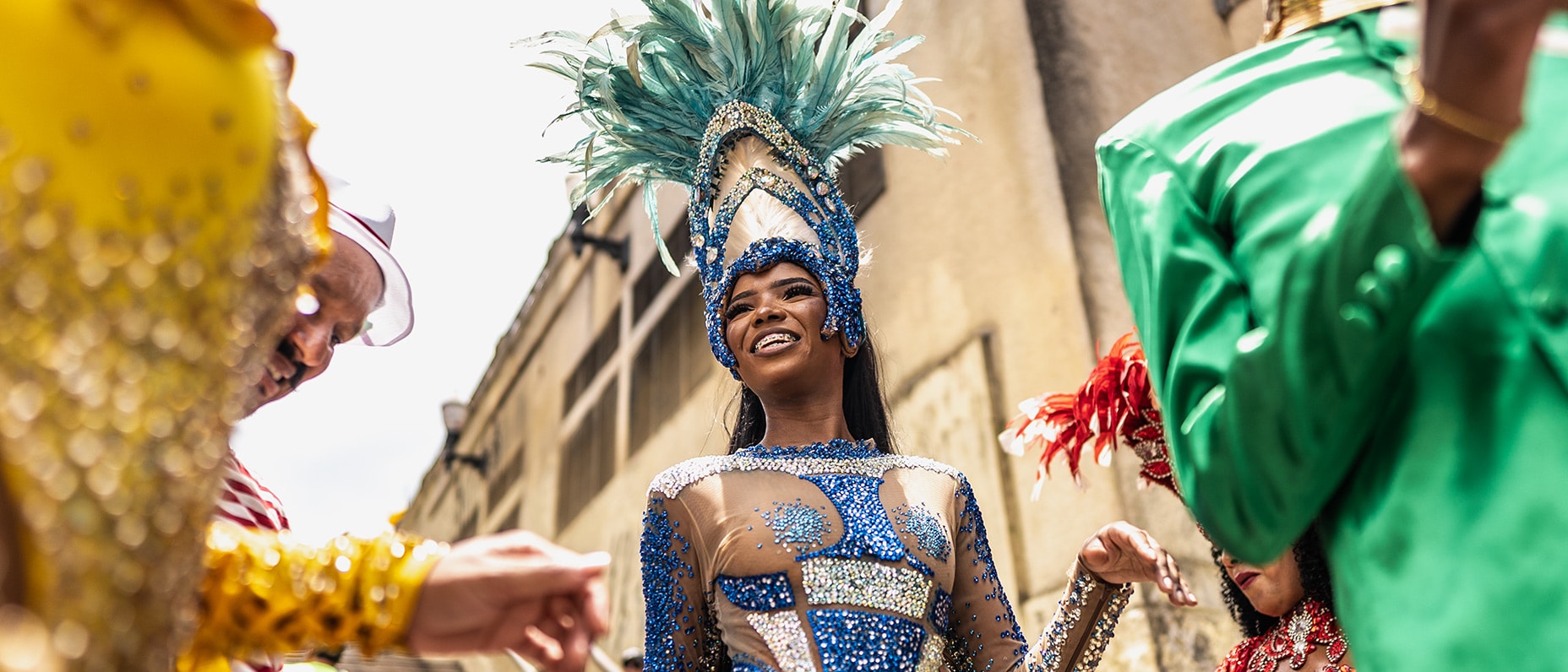 Duas pessoas sorrindo na praia ensolarada brincando com uma bola. O mar e as montanhas formam um cenário vibrante e sereno.