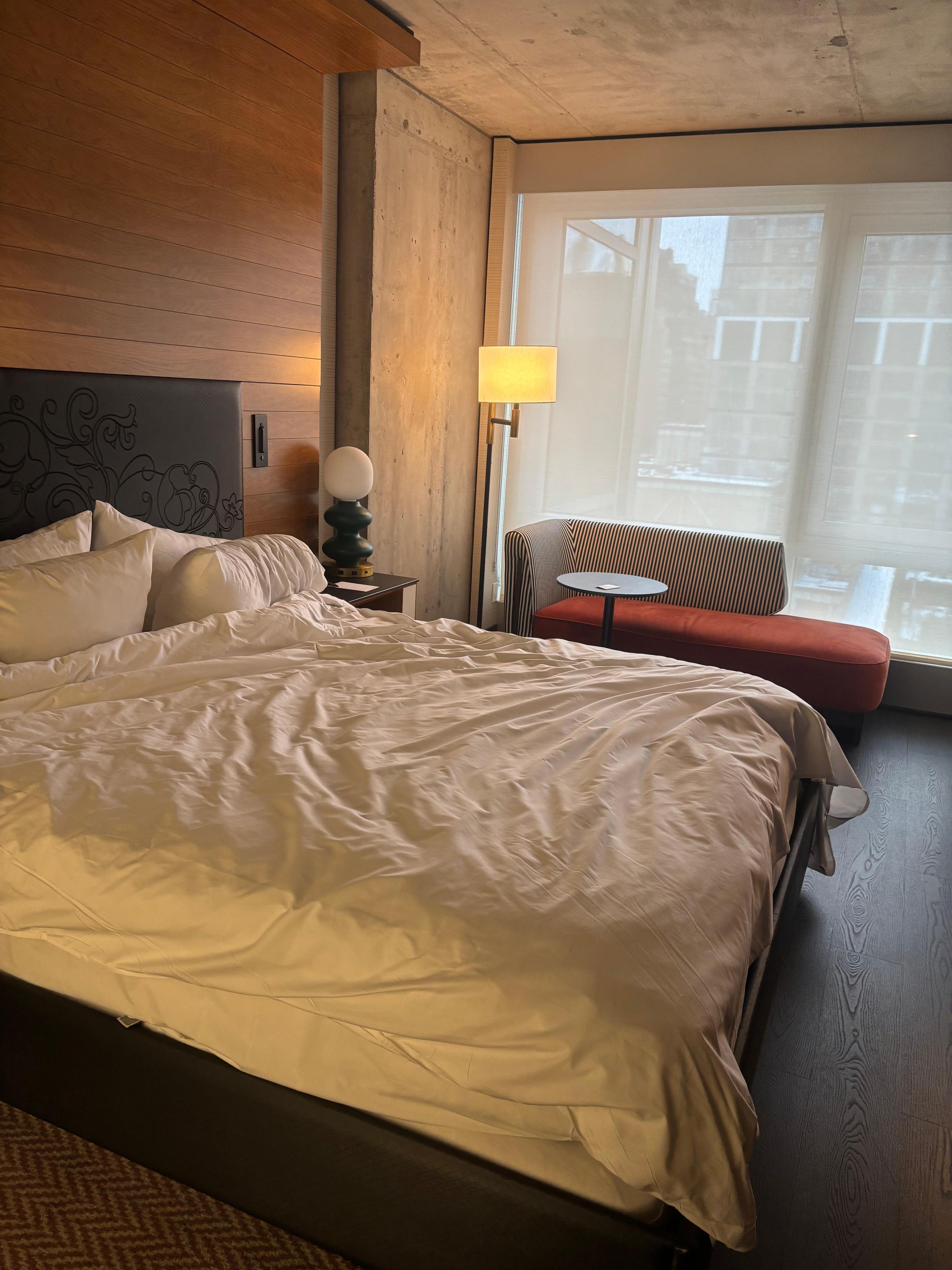 Spacious room with lounging sofa & cocktail table. Along wall opposite bed is an extended counter with desk/ chair  , wall mounted tv & bench. 