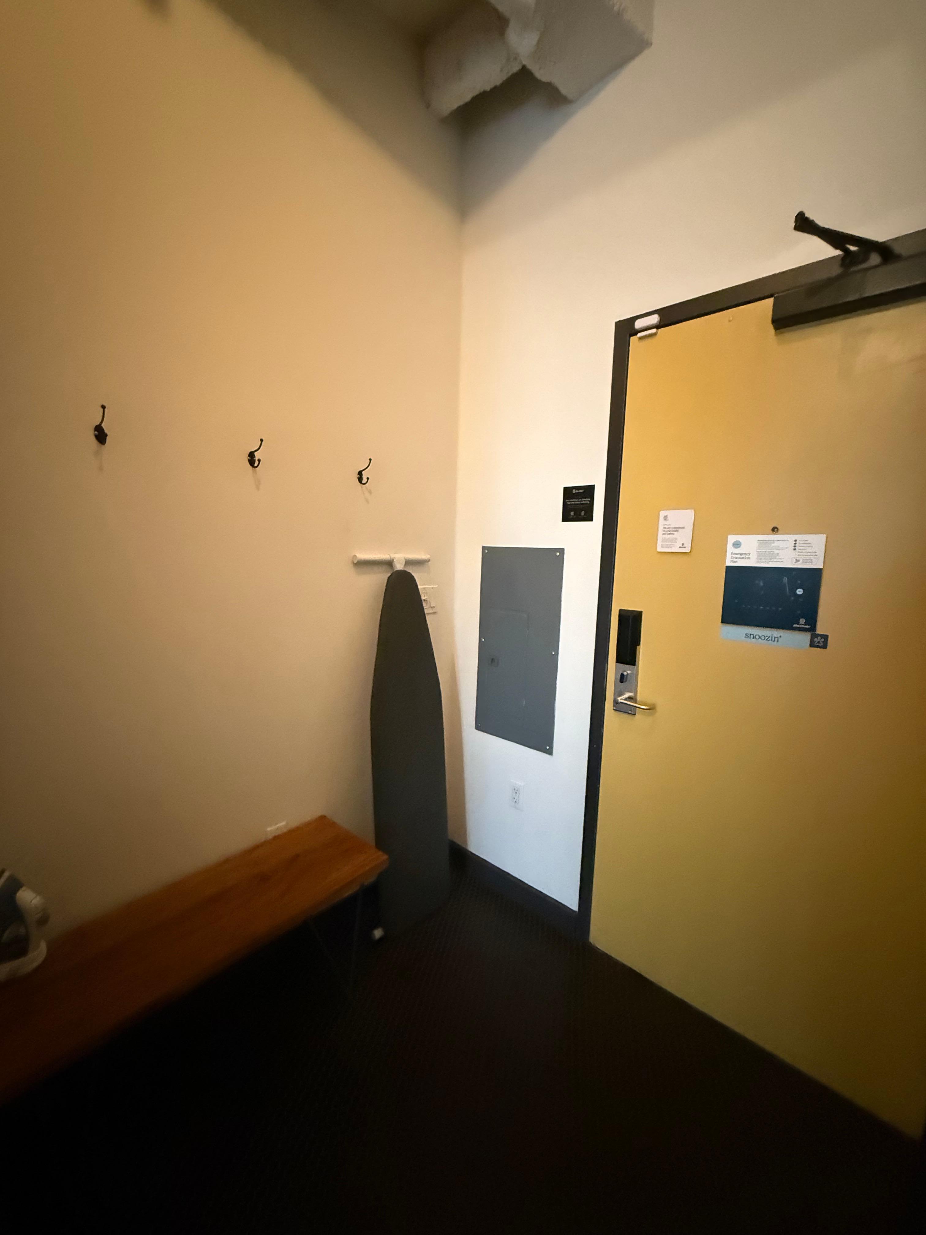 Front door with entryway bench, hooks, iron, and ironing board.