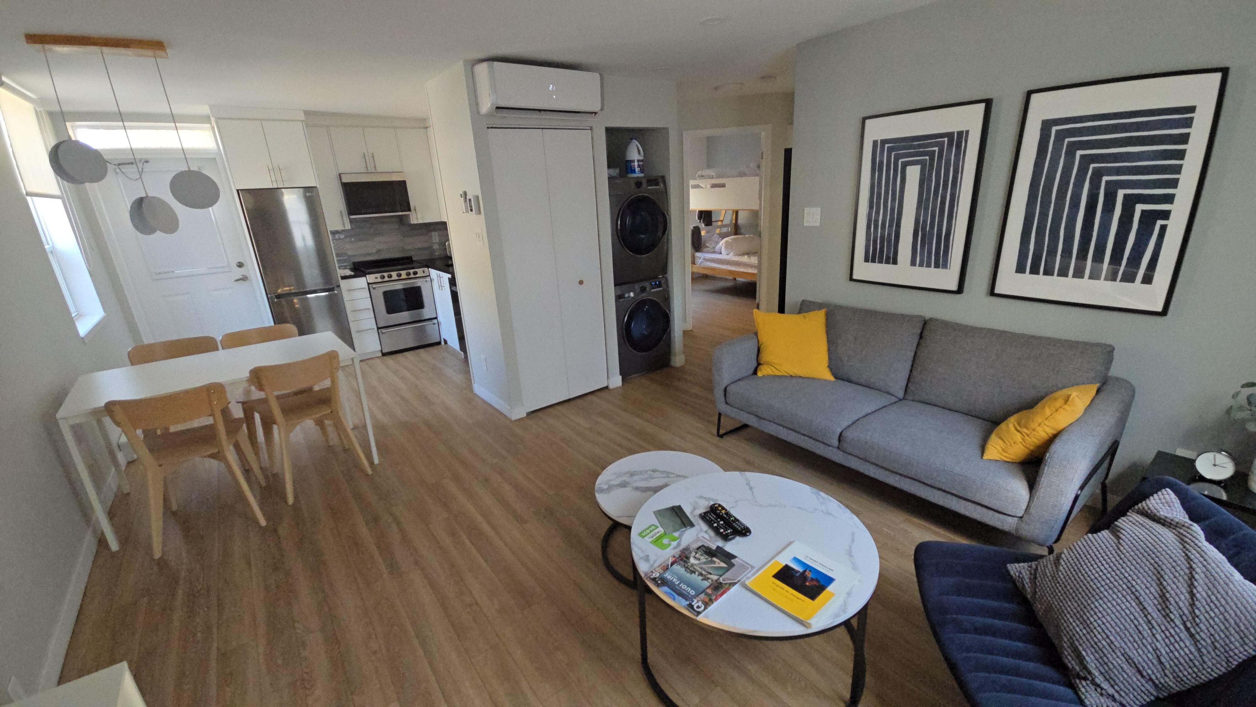 View of living room and kitchen from one end. Washer, dryer available. Air conditioner in middle of room on top.