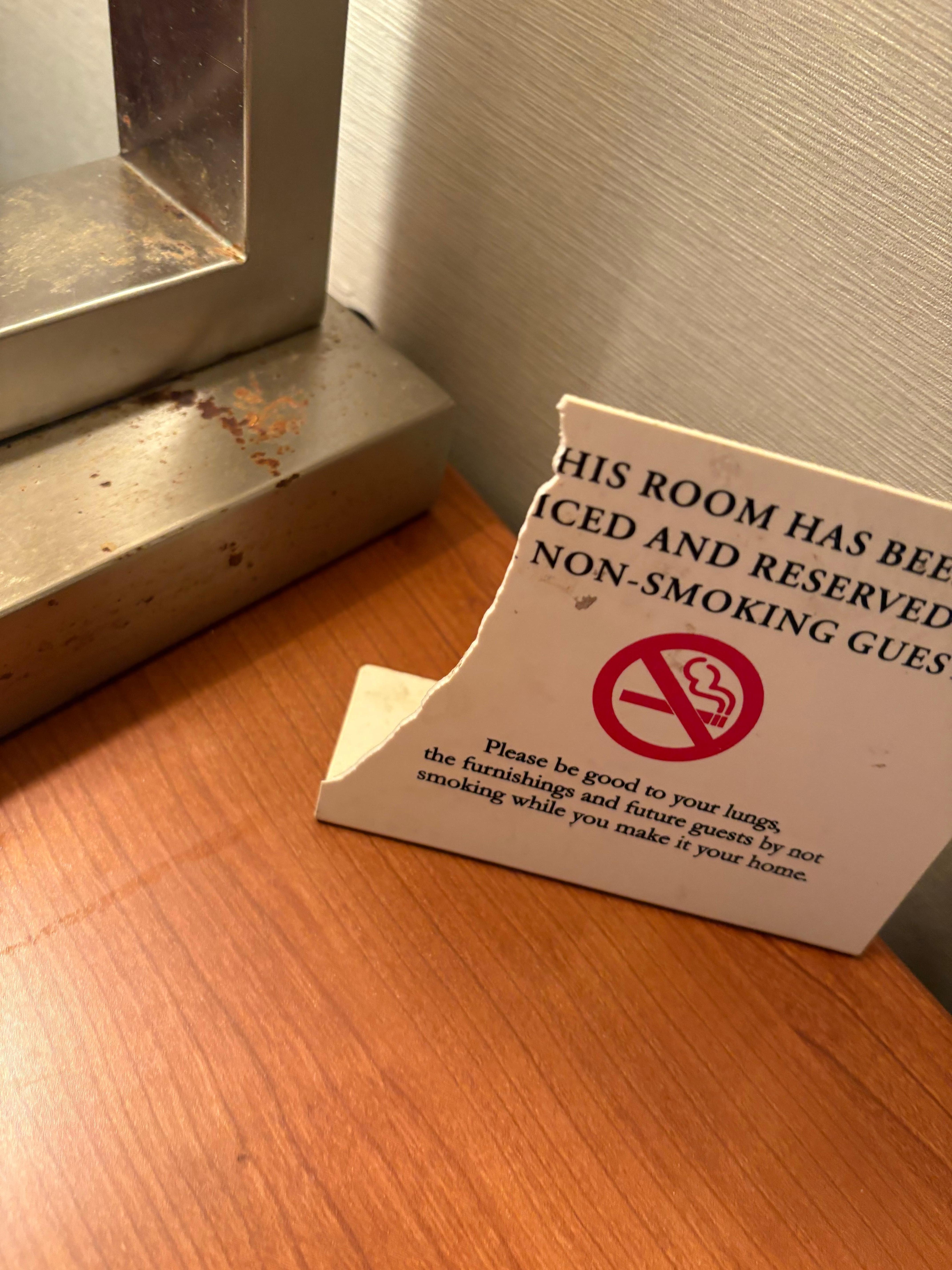 Cracked sign. No smoking with cigarette ash on the counter  