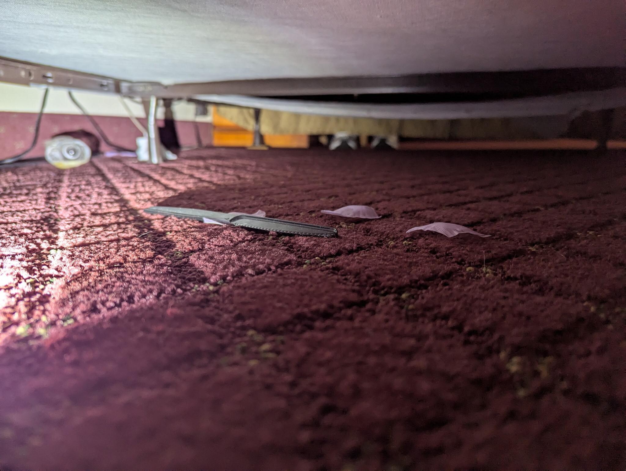 Dirty under bed with dirty bottle and trash