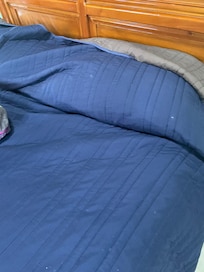 Cama con colcha salpicada con algo y sin extender a la entrega de la habitación.