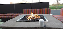 Outdoor gas fire put with decent cushioned seating area, along with tables and chairs.