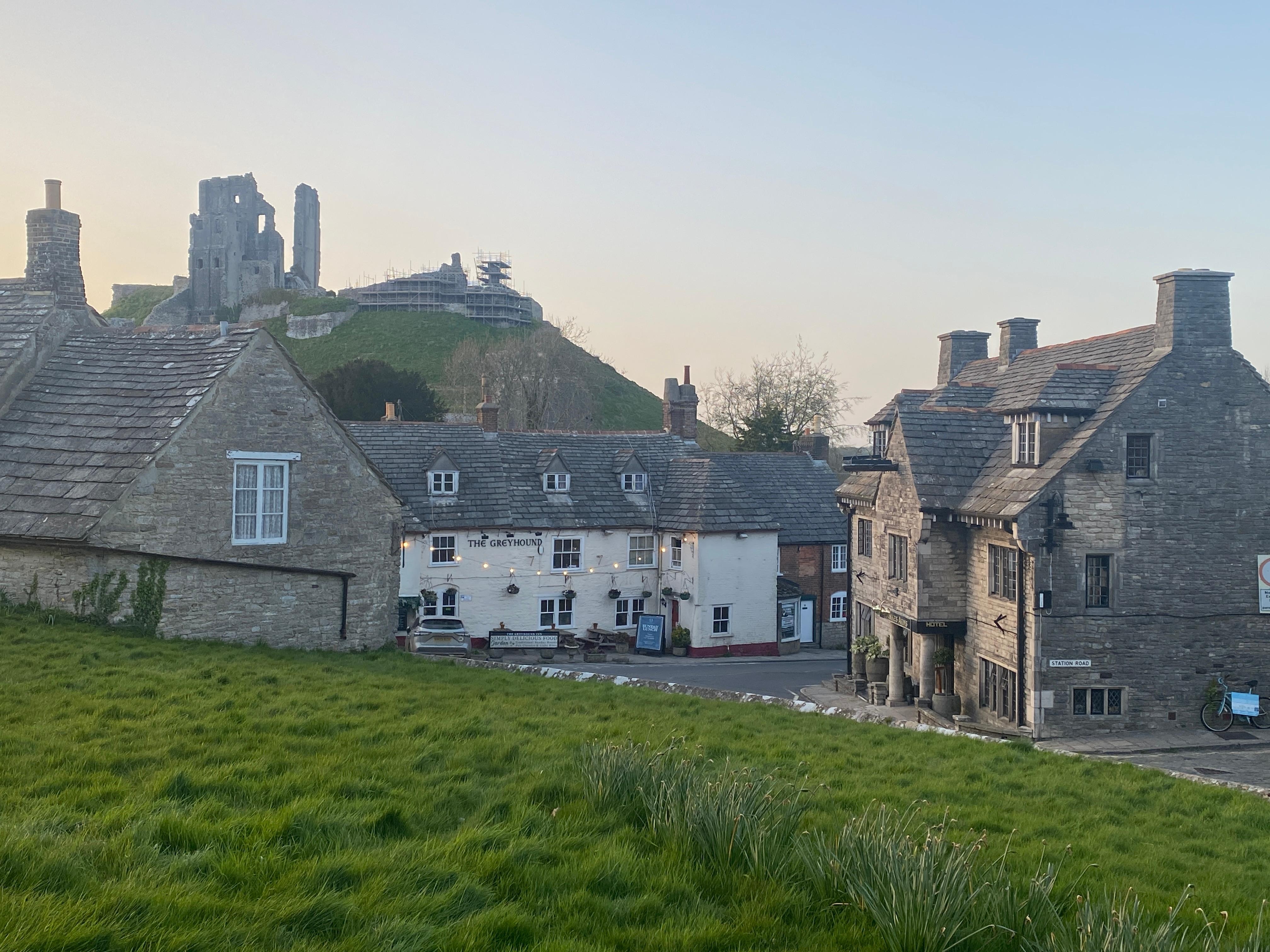 Bankes Arms Hotel in local stone on right. Greyhound Inn painted white on left and castle in the background.
