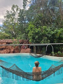 Piscina com cascata e rede para descanso.