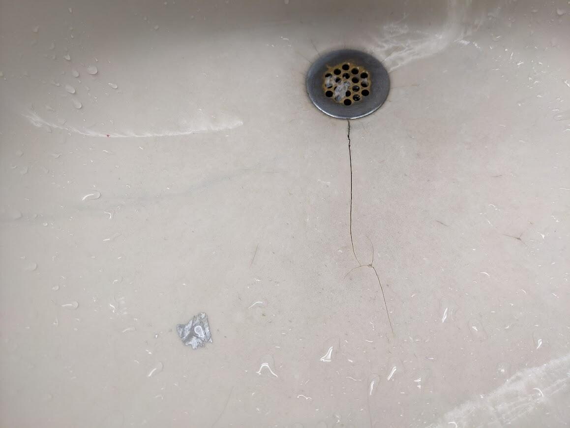 Bathroom sink with crack and a piece of silver tape stuck to the sink.