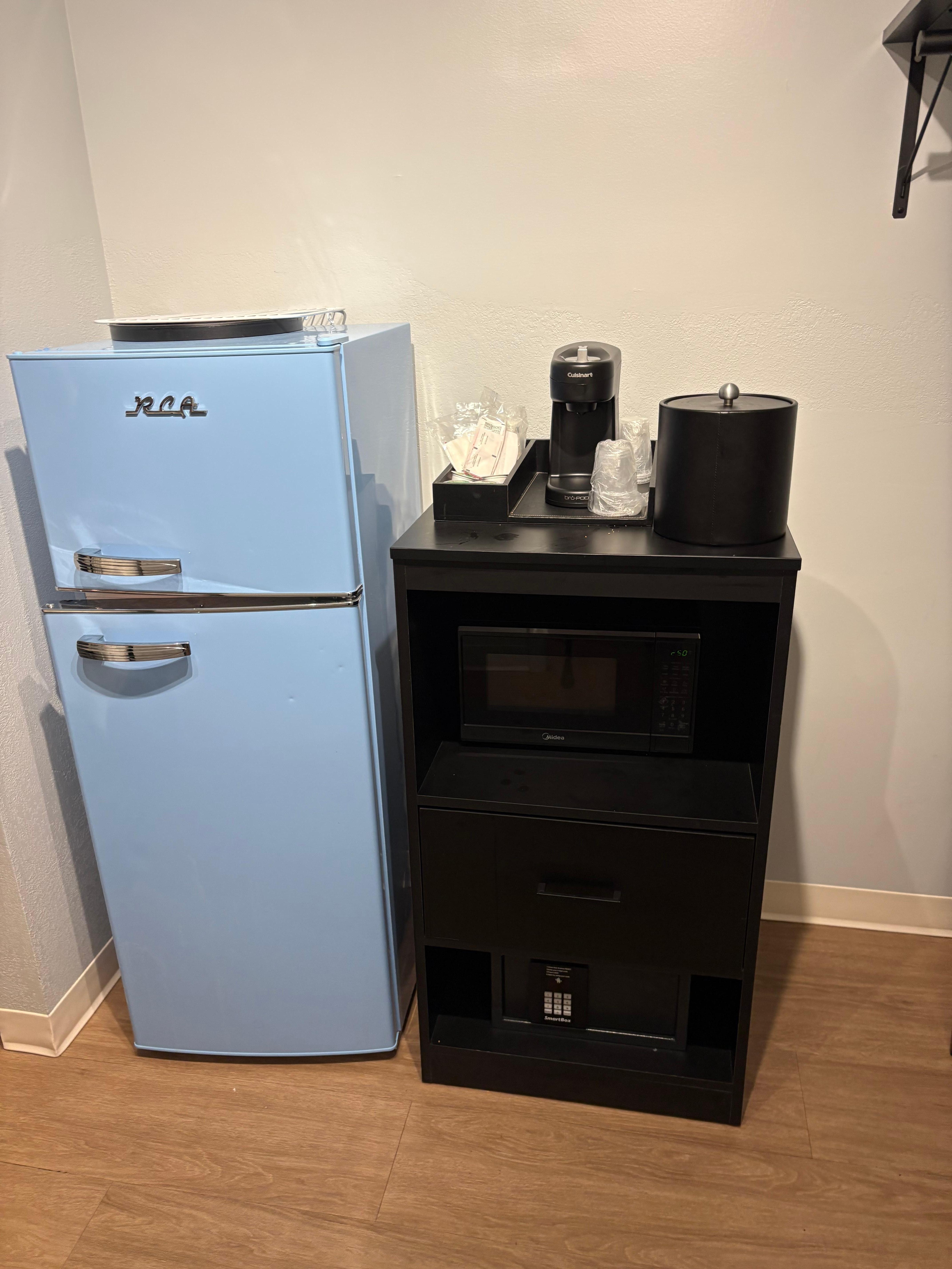 A refrigerator with a freezer, a mini coffee maker and small microwave. 